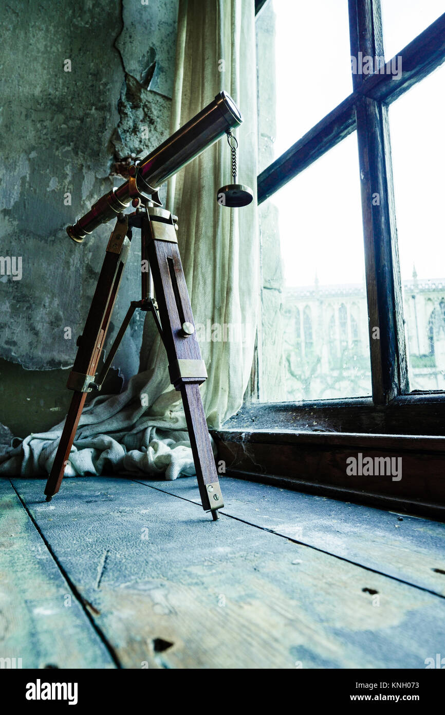 A vintage telescope looking out of an abandoned room window at the ...