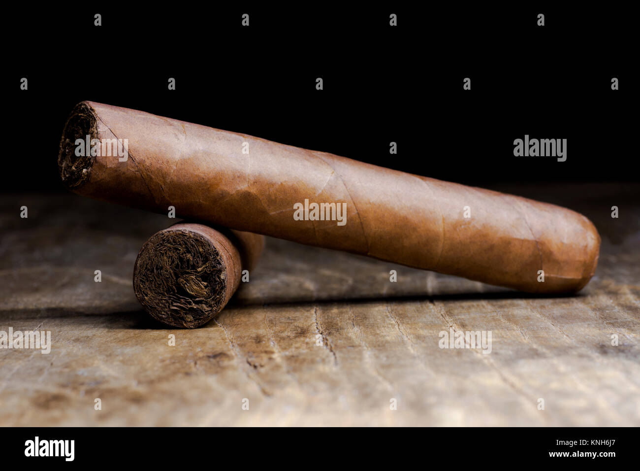 Two Cuban cigars lying on an old wooden table with a blurred background ...