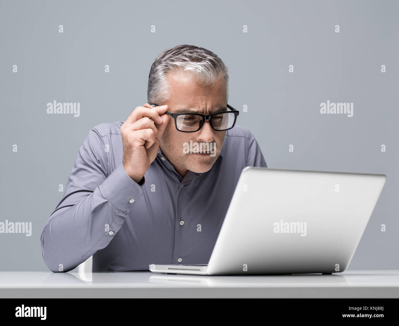 Mature businessman working with a laptop and having vision problems, he ...