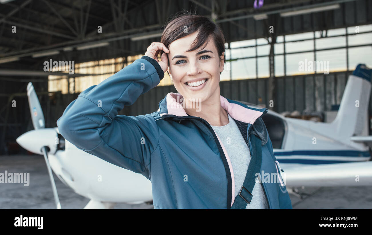 Smiling female pilot posing in the airport hangar, propeller airplane ...