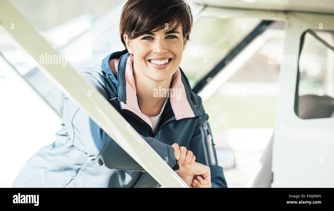 Young pilot woman leaning on an airplane and smiling at camera, travel ...