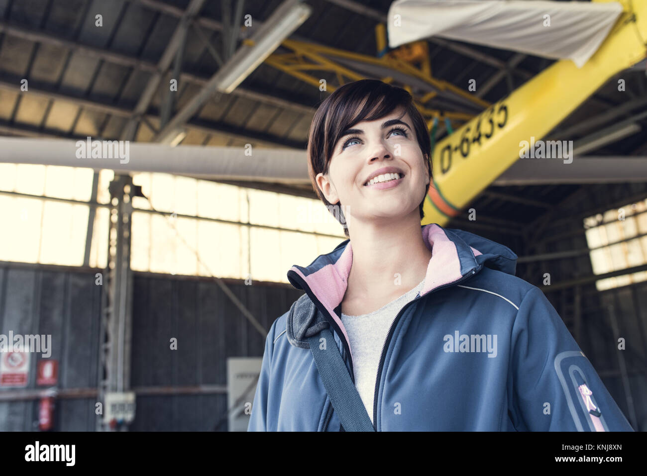 Smiling female pilot posing in the airport hangar, propeller airplane ...