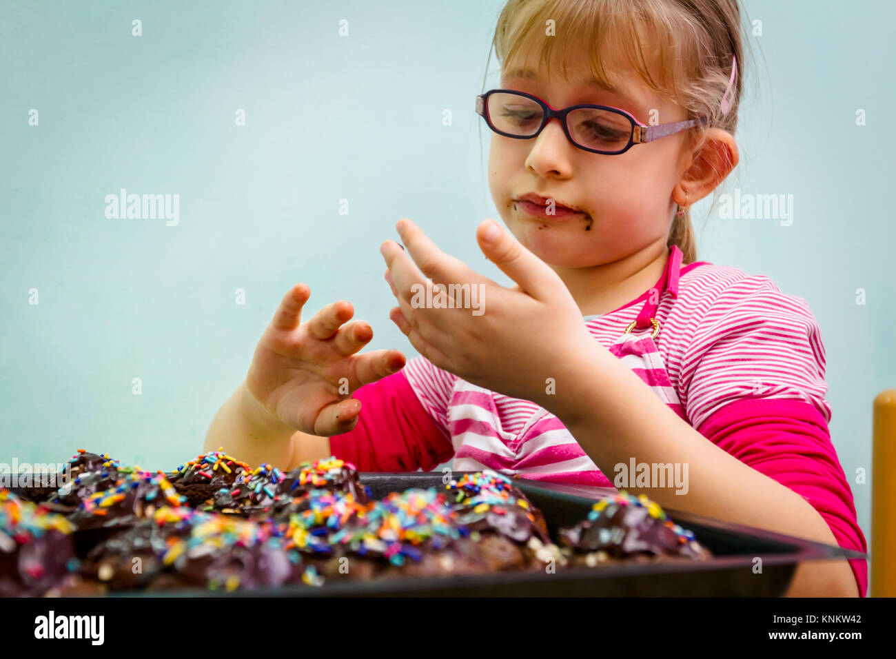 Little cute girl with chocolate on face and hands is eating a decorated ...