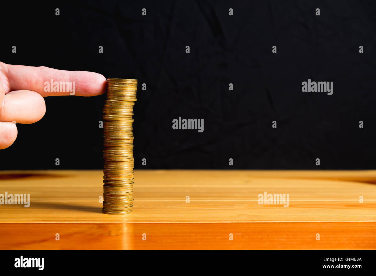 Finger pushing a column of coins on wooden table with black wall, gold ...