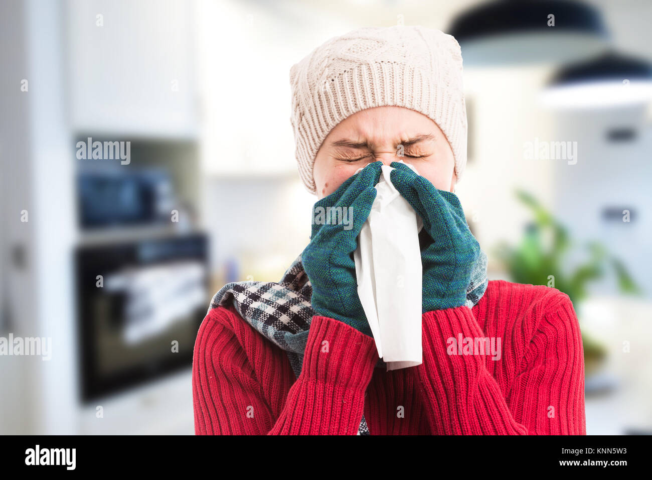 Woman indoors blowing her nose as cold influenza concept with warm ...