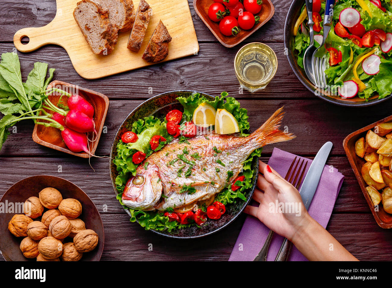 Woman hand serving grilled fish on table with colorful dishes Stock ...