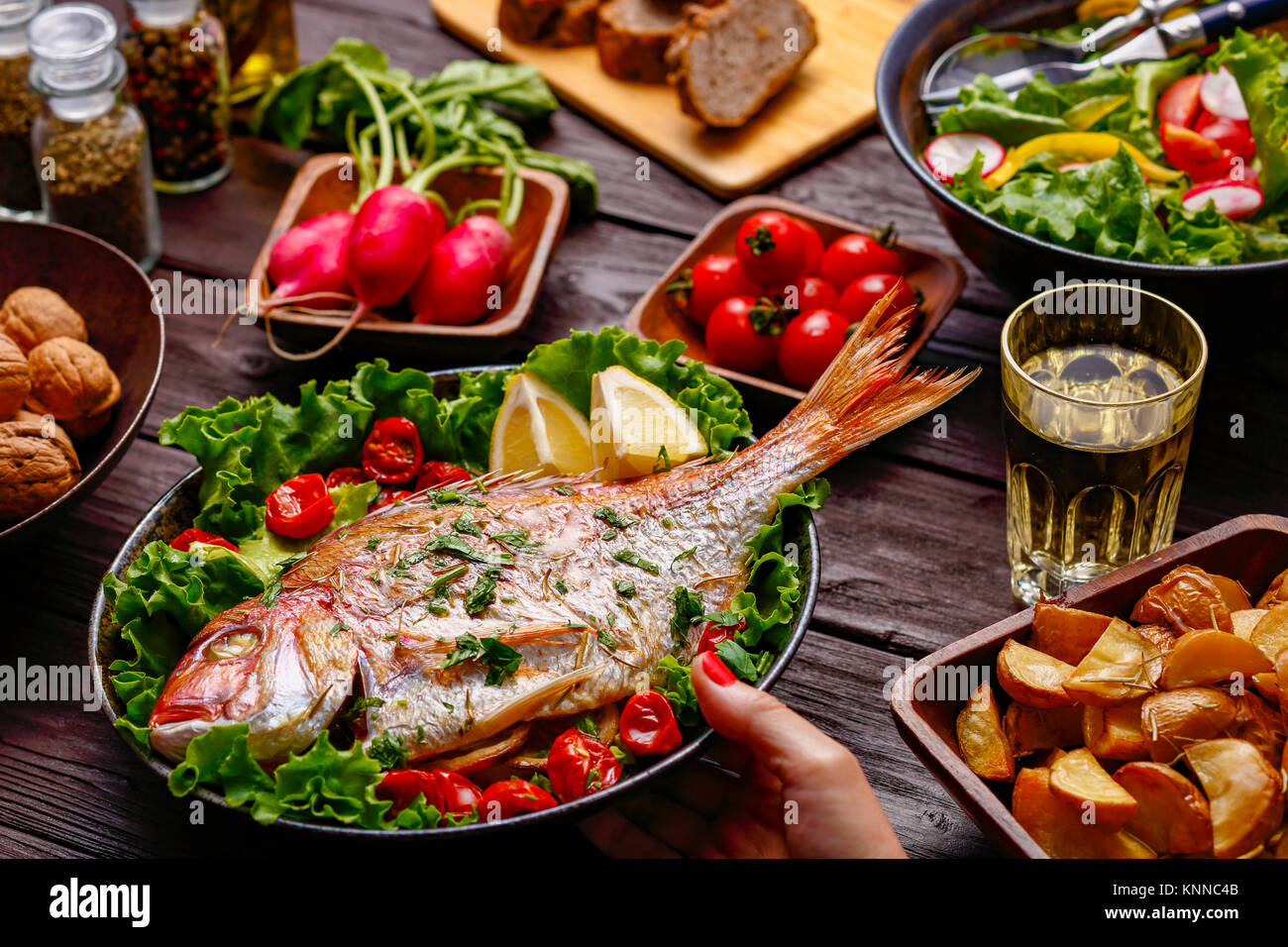 Woman hand serving grilled fish on table with colorful dishes Stock ...