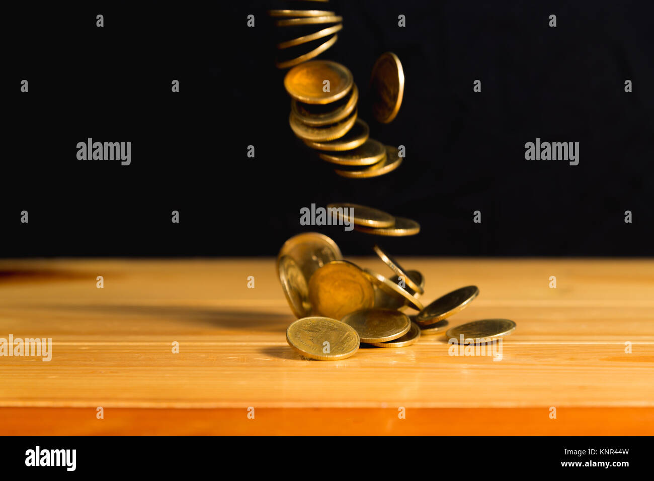 Falling gold coins money on wooden table with black wall, copy space ...