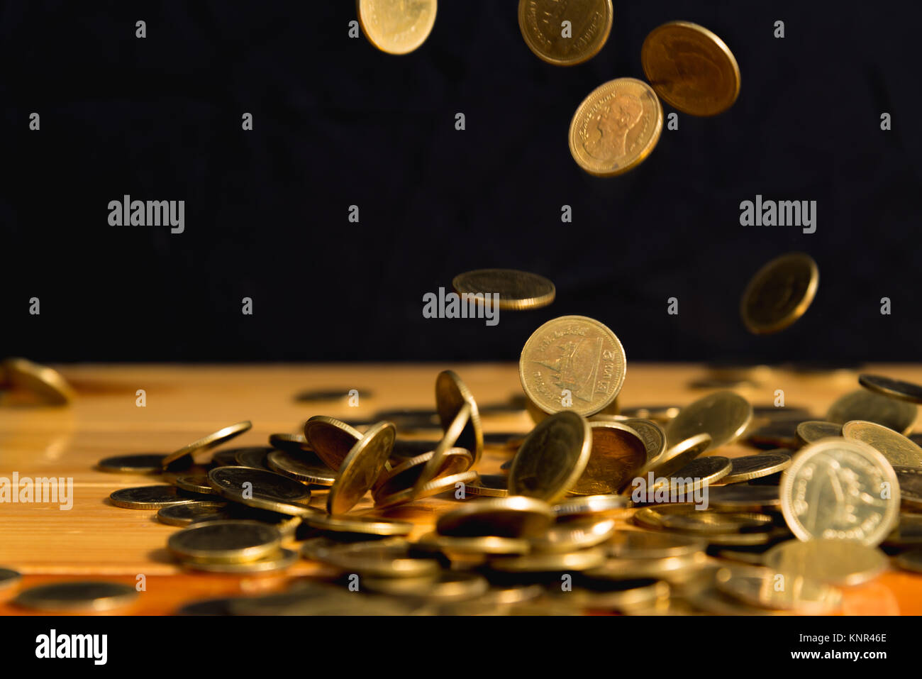 Falling gold coins money on wooden table with black wall, copy space ...