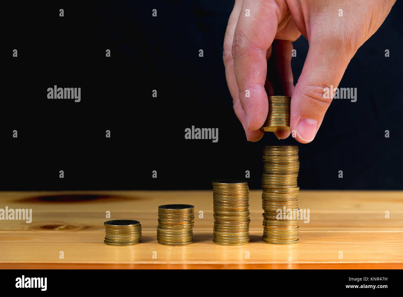 Hand put money gold coins to stack of coins on wooden table with black ...