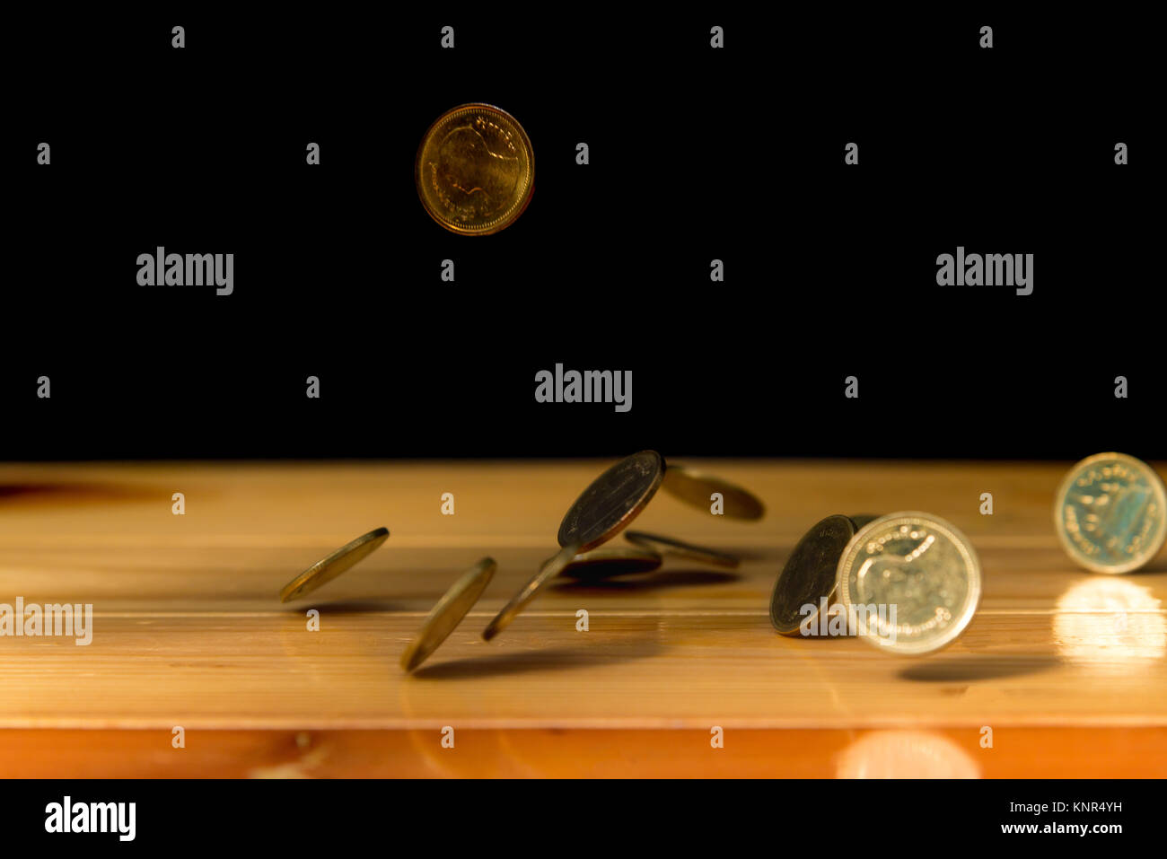 Falling gold coins money on wooden table with black wall, copy space ...