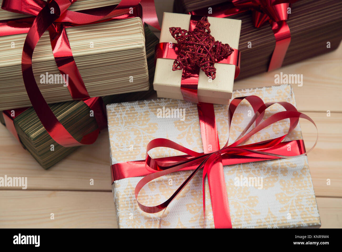 Light patterned gift boxes with red metallic ribbons on a light wooden ...