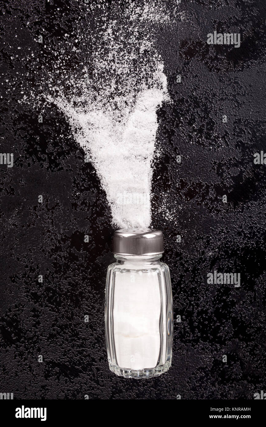 Salt shaker with salt on black background from above Stock Photo - Alamy