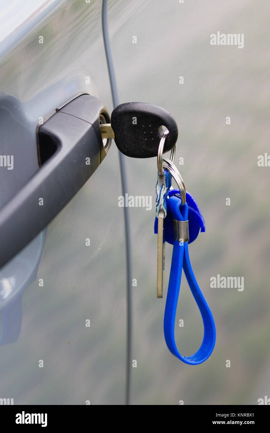 Worn old fashioned car keys with blue keychains in a lock of gray car ...