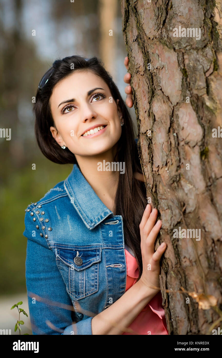 Junge Frau steht neben Baumstamm - woman is standing next to tree trunk ...