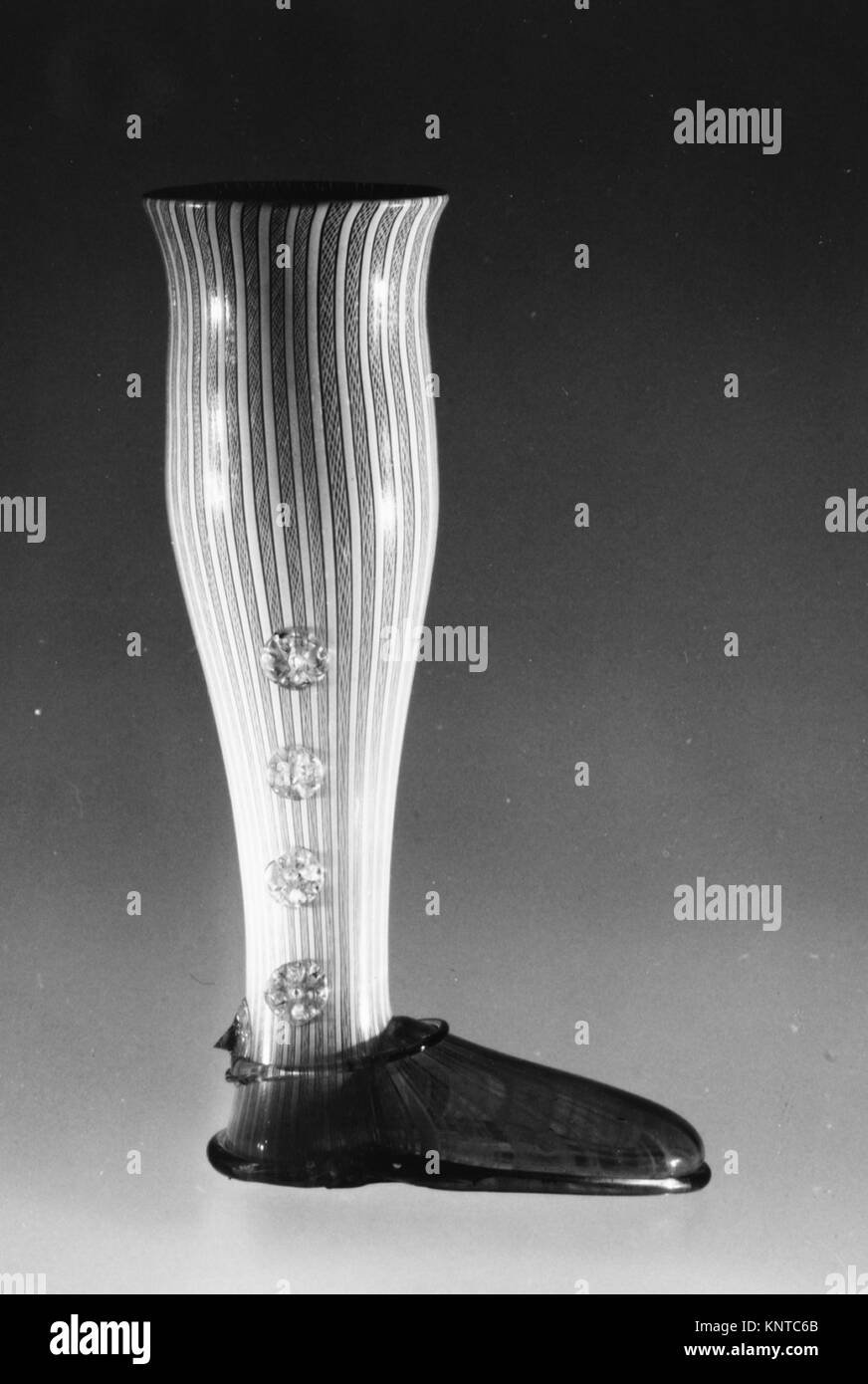 A colorless (gray) and opaque white nonlead glass boot-shaped vessel ...