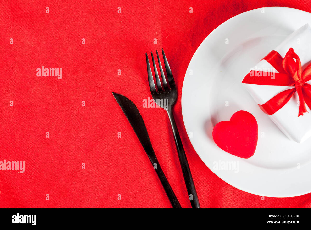 Valentine's day table setting with plate, fork, knife, gift box and red ...