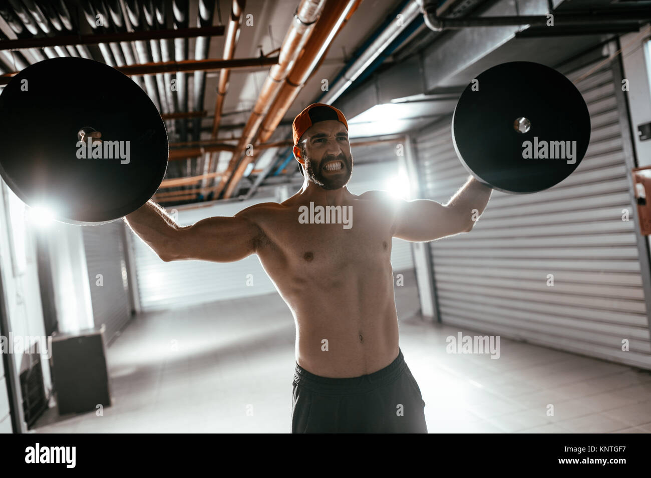Young muscular man doing hard exercise with weights for shoulders on ...
