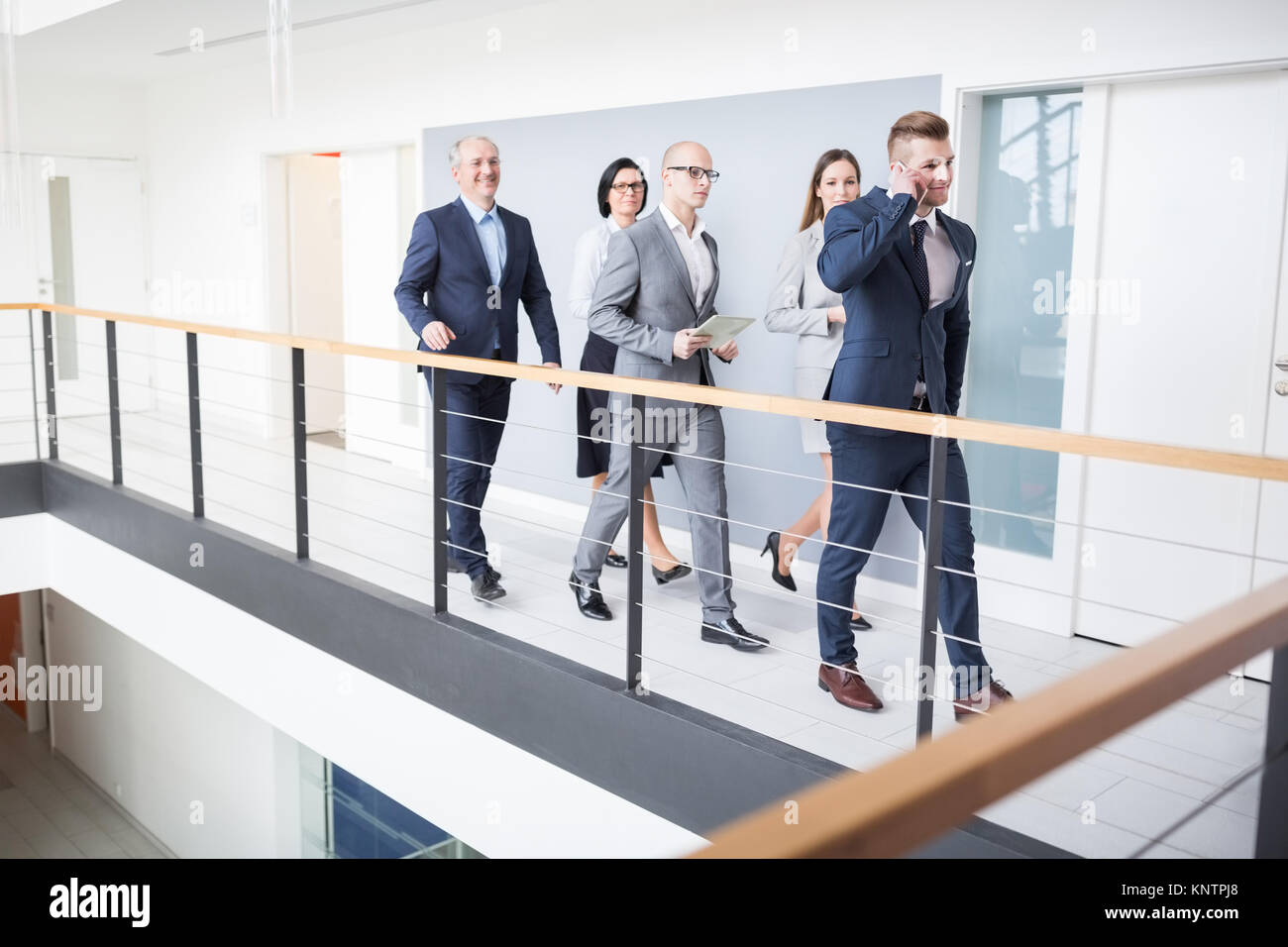 Full length of confident business team walking on corridor by railing ...