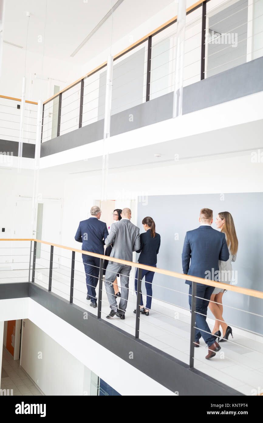Full length of business people walking by railing on corridor in office ...