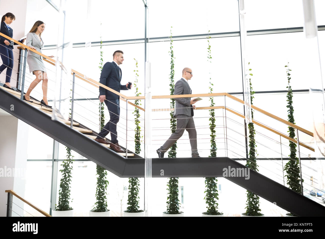 Full length of male and female business people moving downstairs in ...