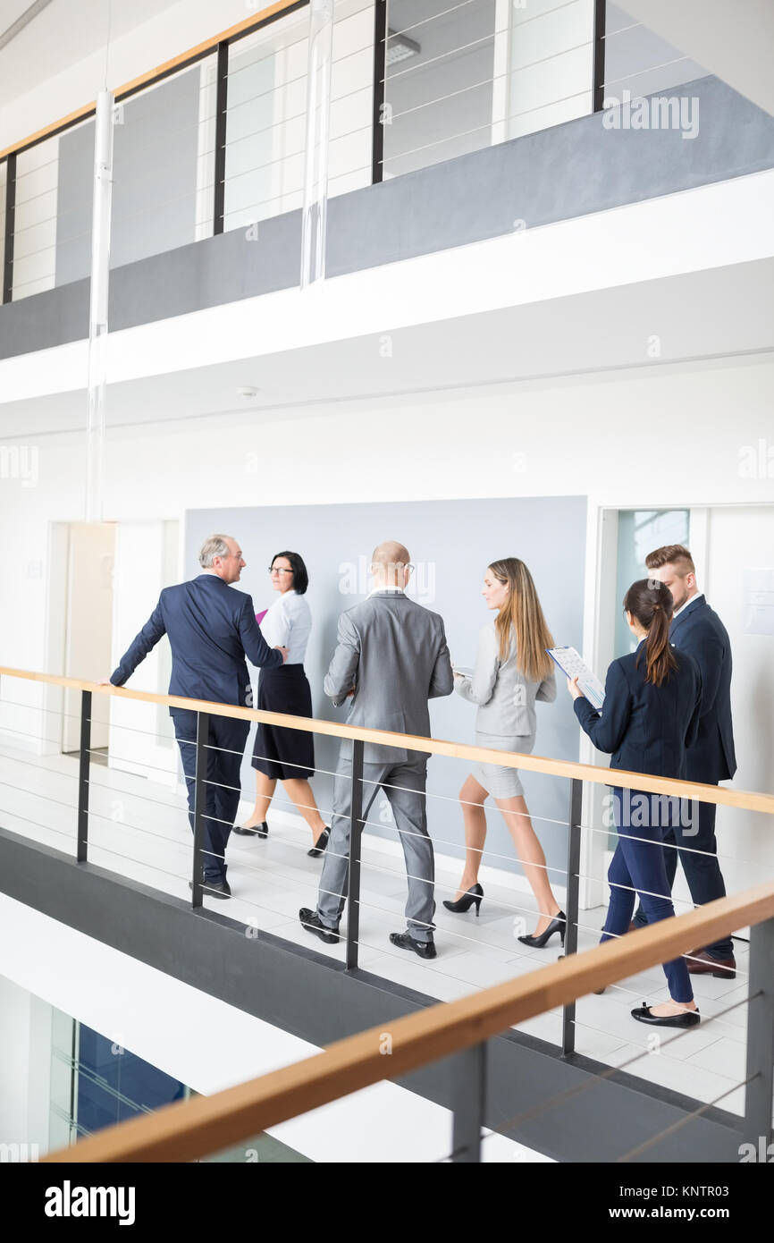Full length of business people discussing while walking by railing on ...