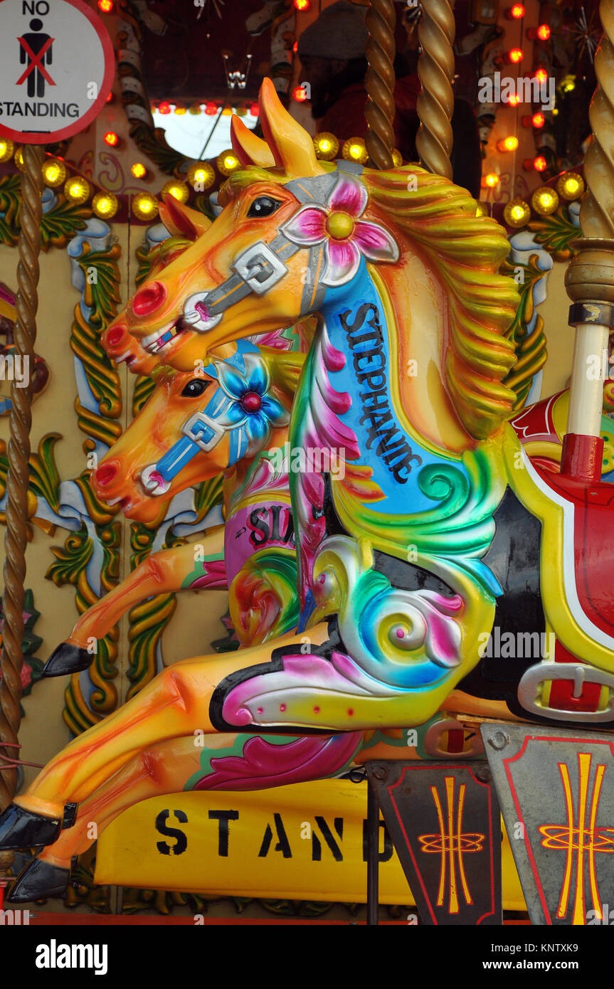 Brightly coloured painted fairground carousel horses on golden poles ...