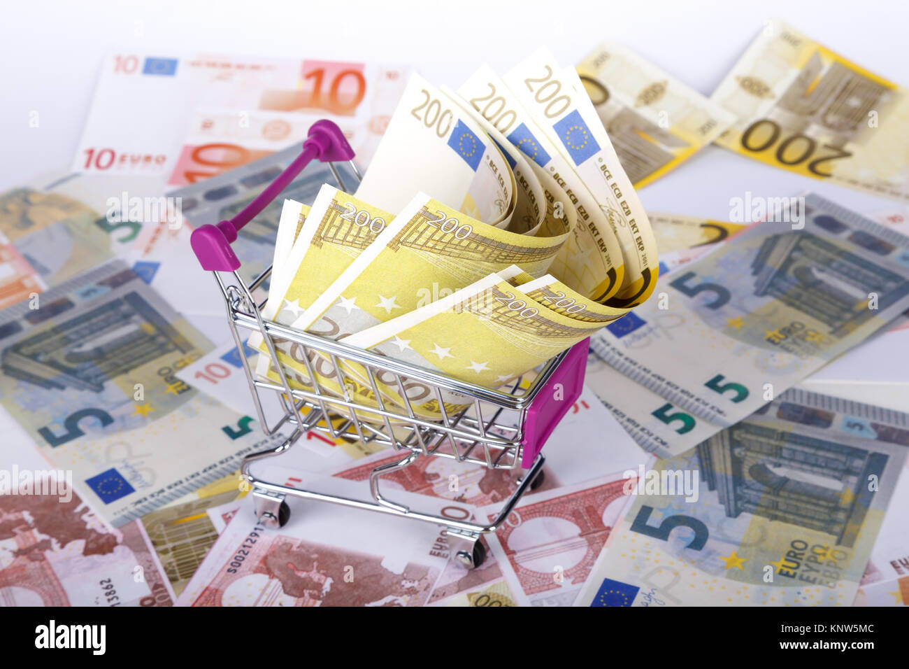 Stack of Euro banknotes with shopping cart in money consuming concept ...