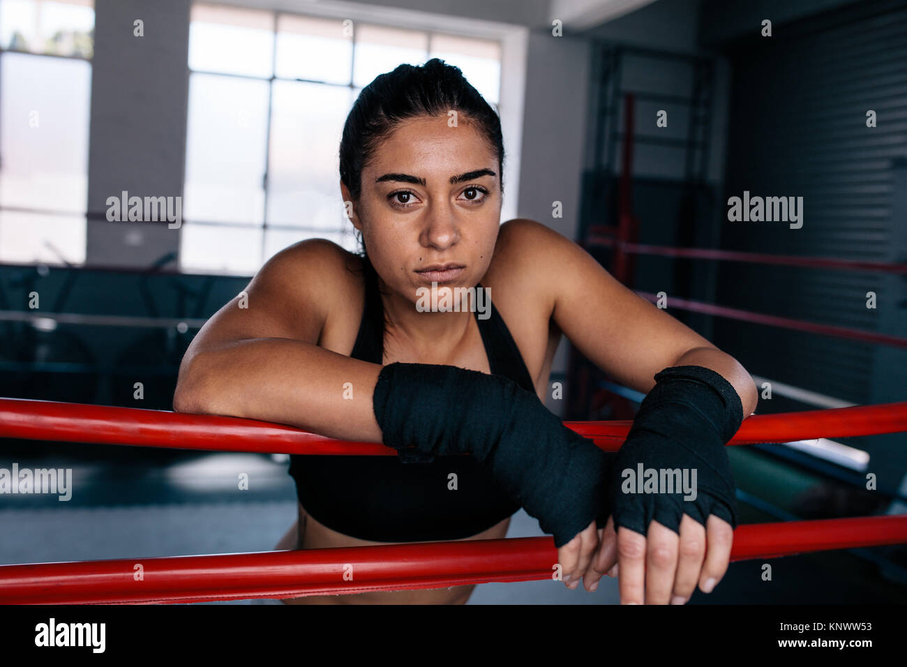 Female boxer standing inside a boxing ring. Boxer resting her arms on ...