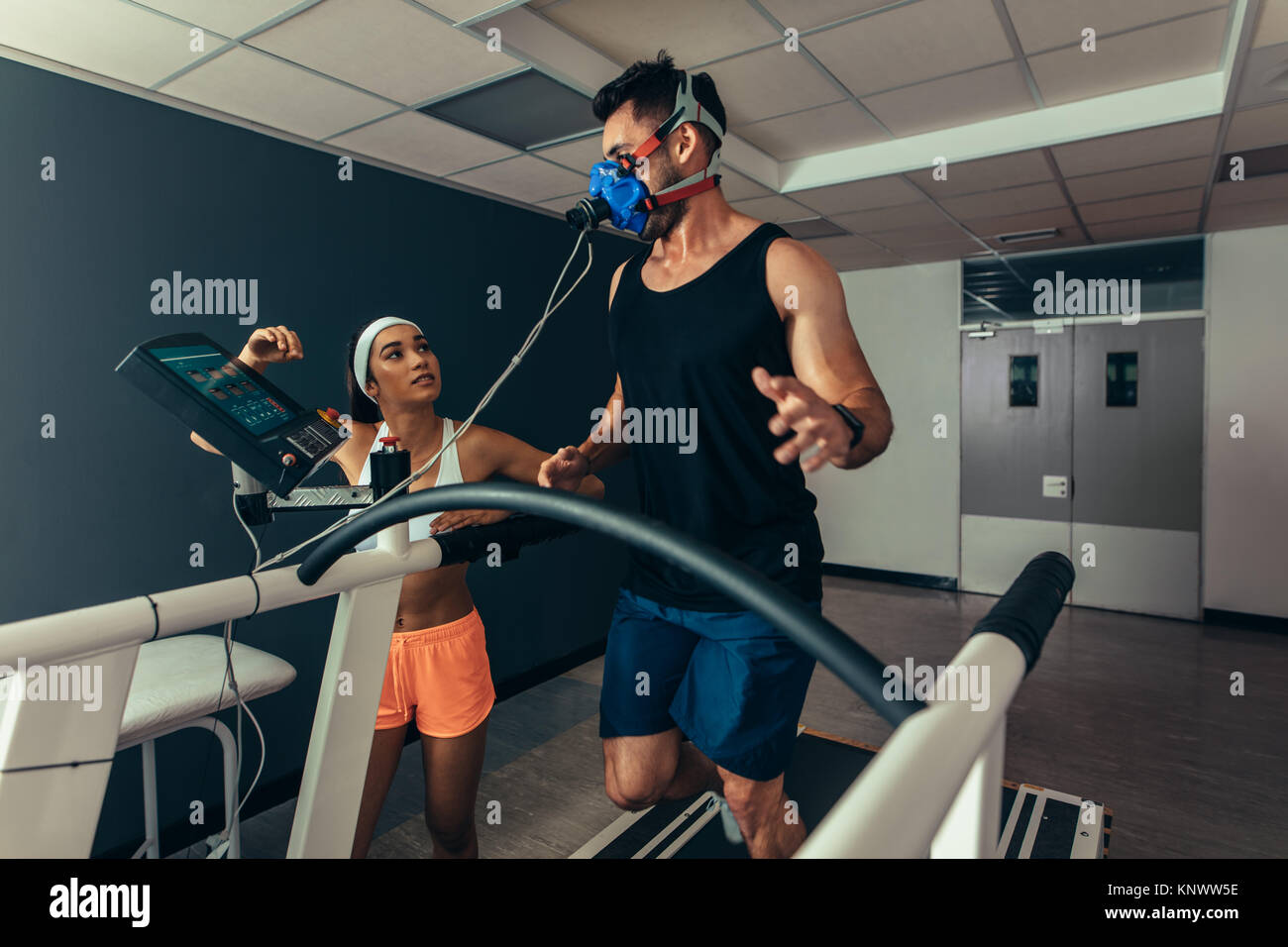 Runner with mask on treadmill in laboratory with woman standing by ...