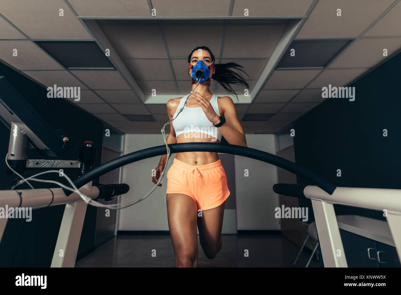 Fit young woman running on treadmill with a mask. Athlete examining her ...