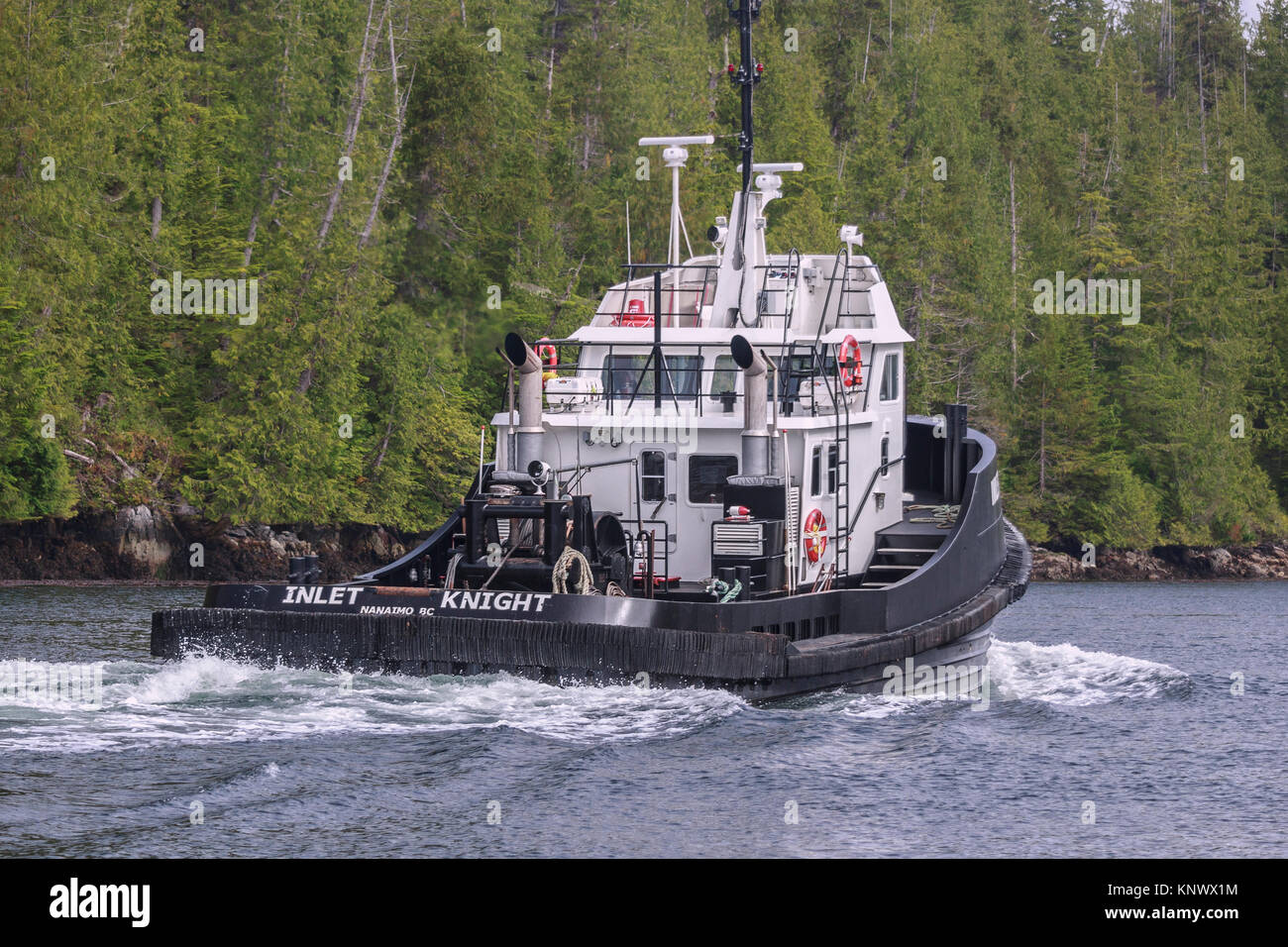 The tug boat "Inlet Knight" motors alongside the forested shore of ...