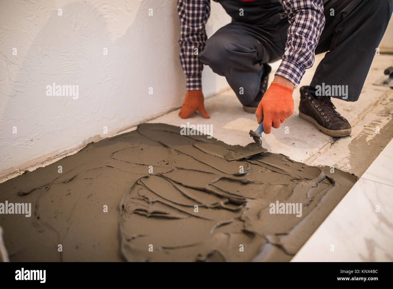 Troweling mortar onto a concrete floor in preparation for laying white ...