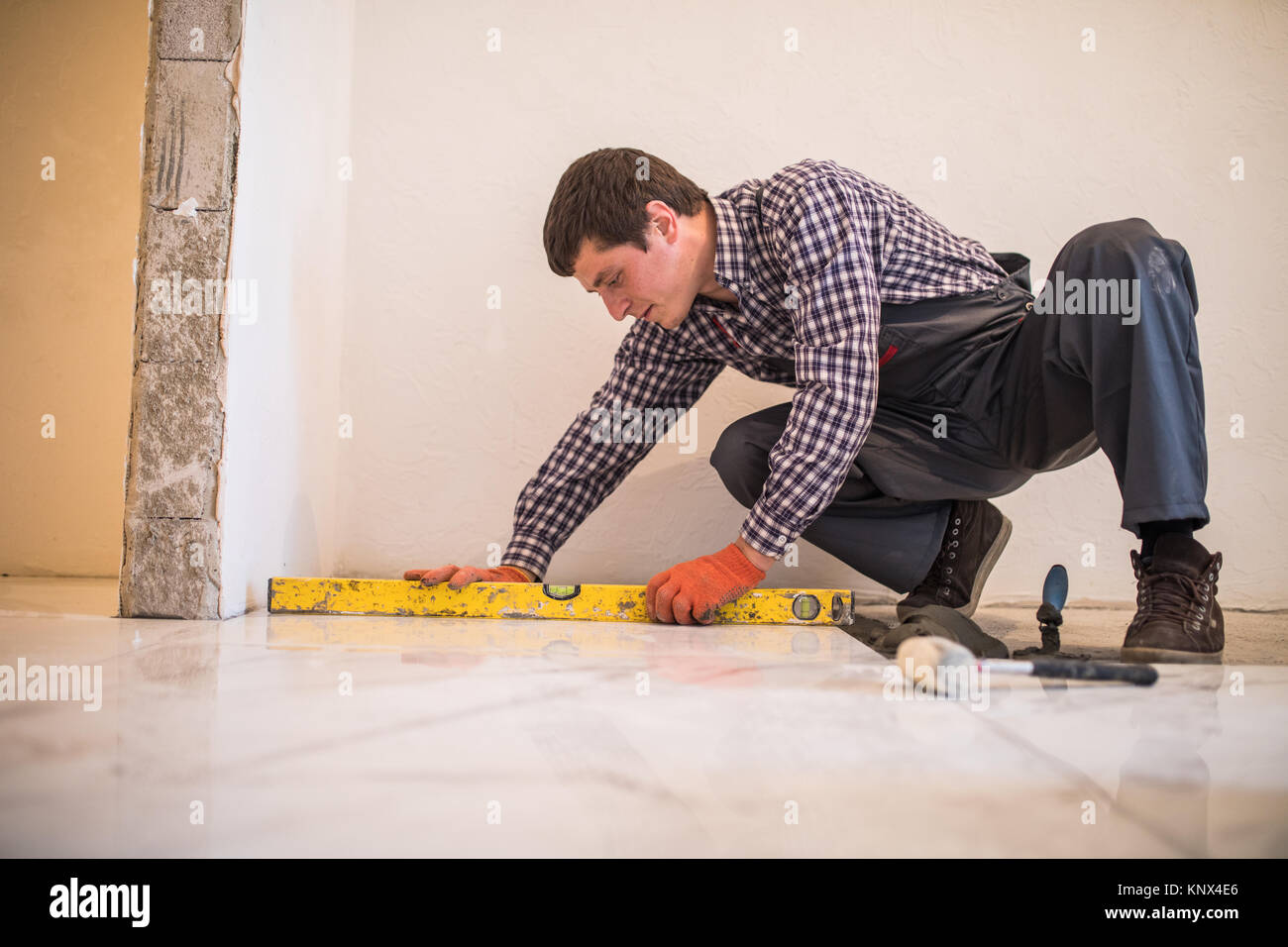 Home tile improvement - handyman with level laying down tile floor ...