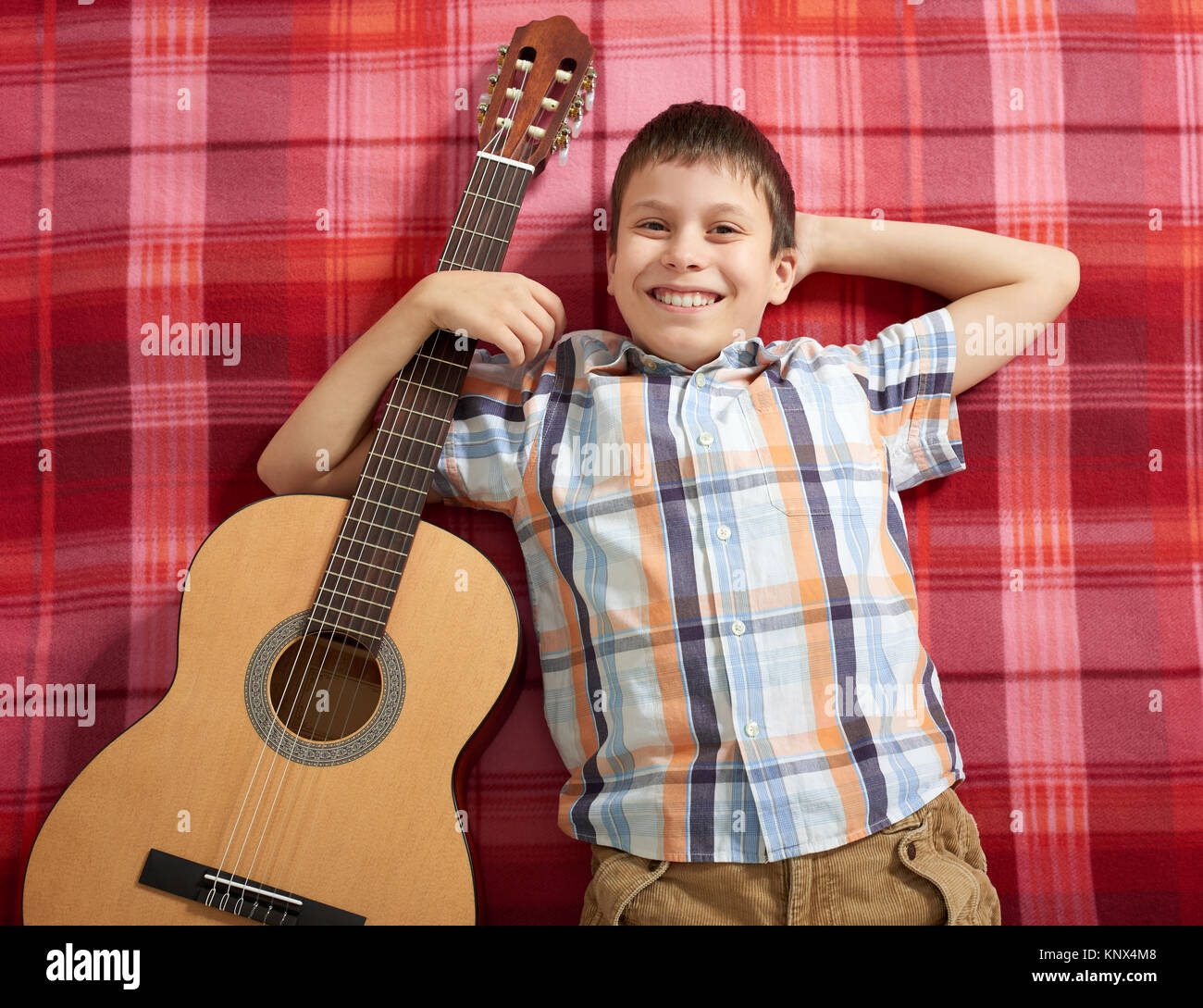 boy playing music on guitar, lies on a red checkered blanket, top view ...