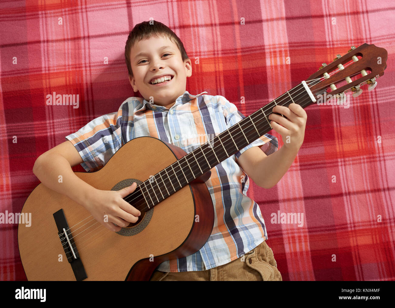 boy playing music on guitar, lies on a red checkered blanket, top view ...