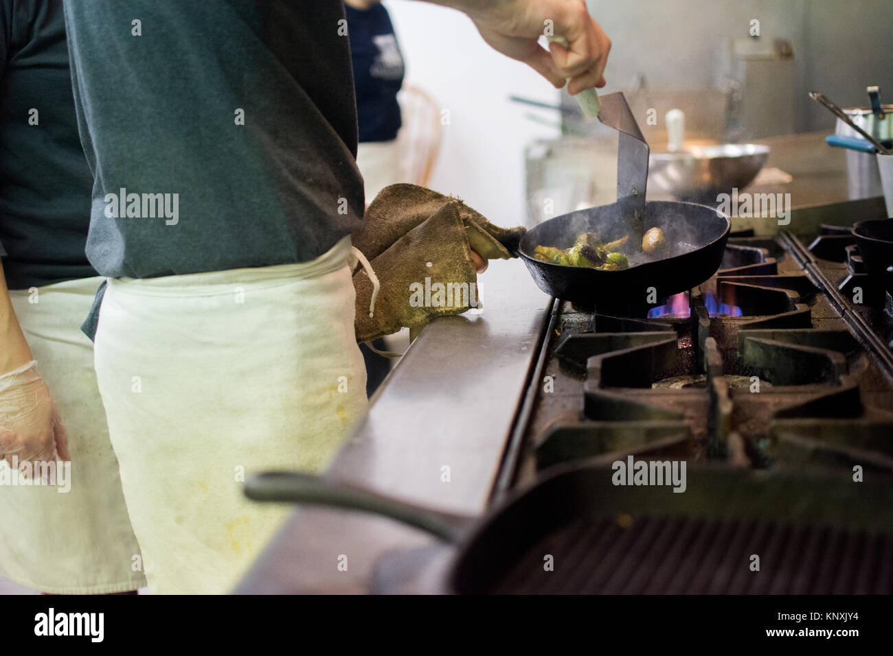 A chef cooks brussel sprouts in a cast iron pan at a farm-to-table ...