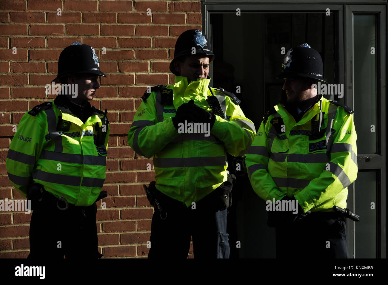 Three policemen in high-vis jackets stand in hard afternoon sunlight ...