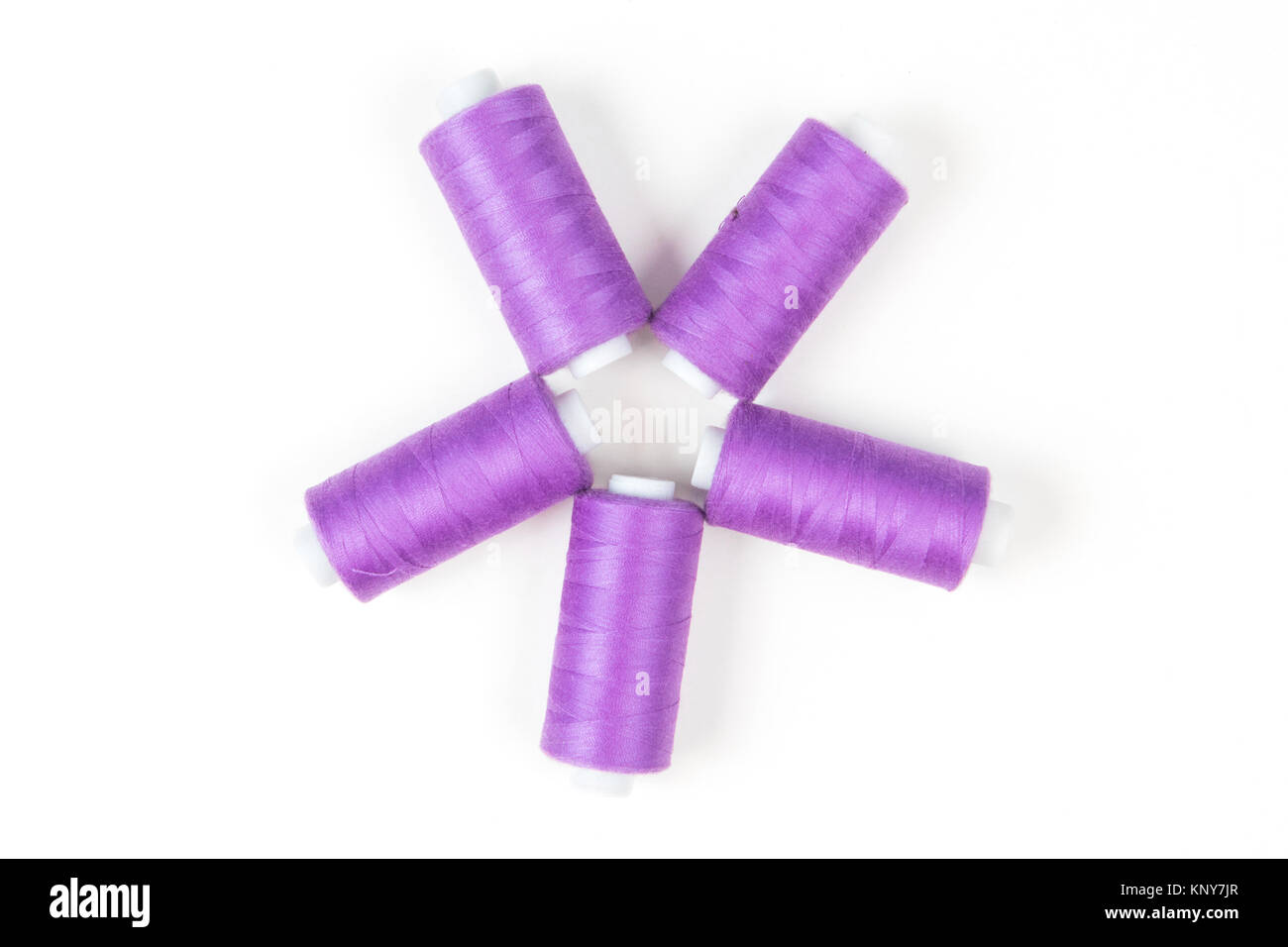 Five orchid purple sewing threads laying in a circle on a white ...