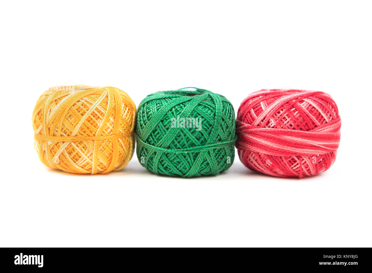 Three colored sewing threads in a row on a white background. Blue, green and yellow threads ...