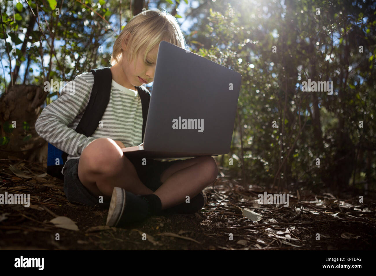 Little girl with a backpack sitting on ground using her laptop in the ...