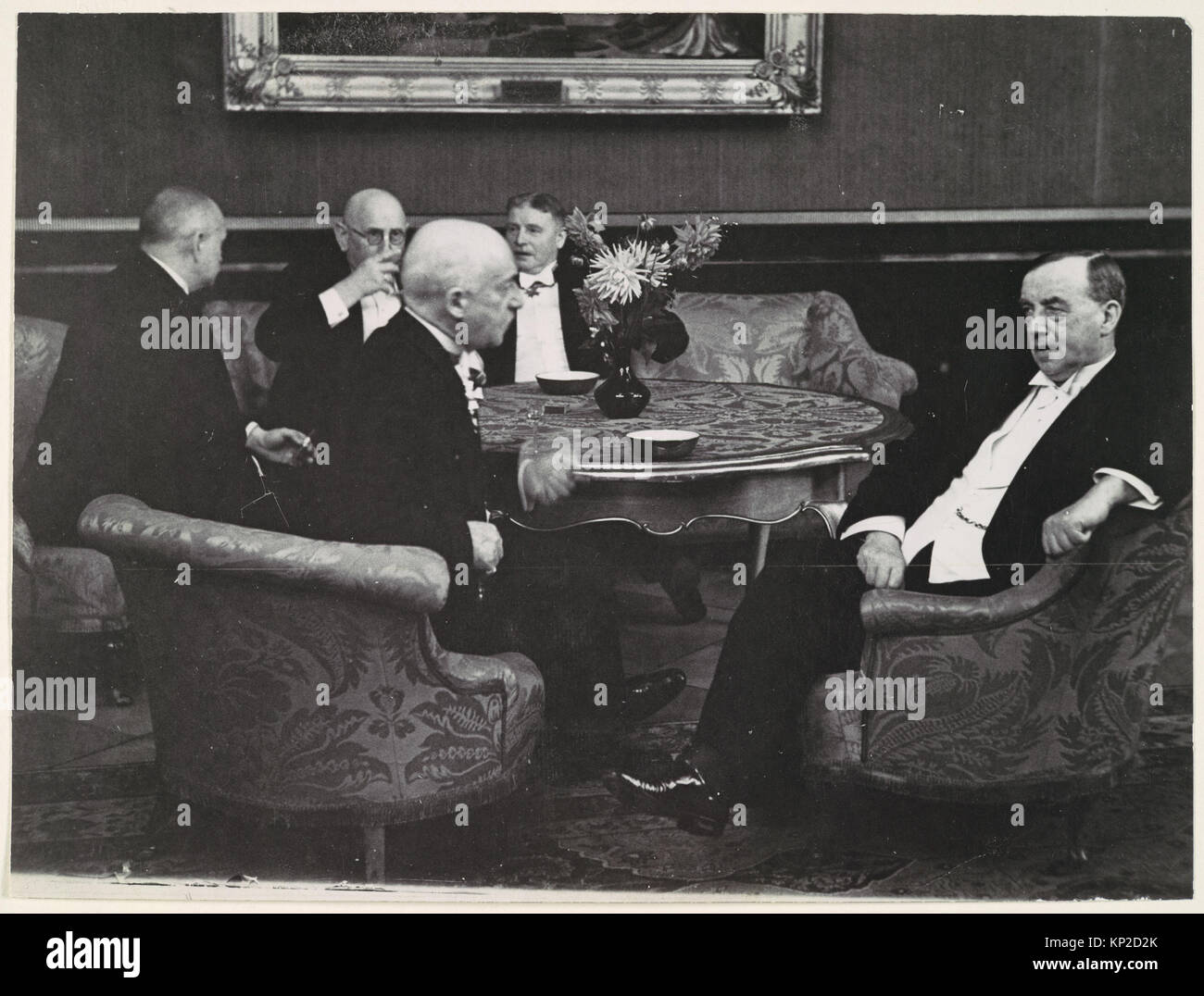 Five gentlemen sit around a table engaged in conversation. The interior ...