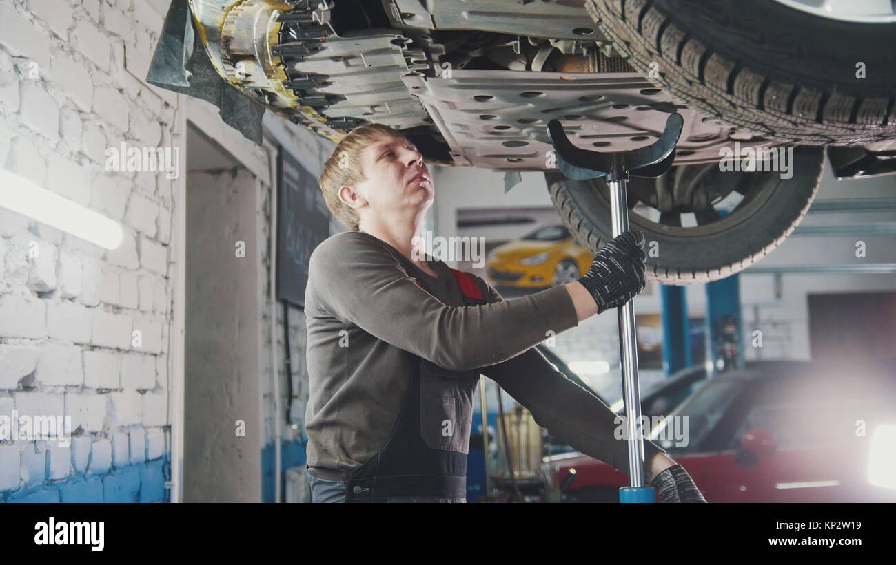 Mechanic unscrewing parts of automobile's bottom under lifted car Stock ...