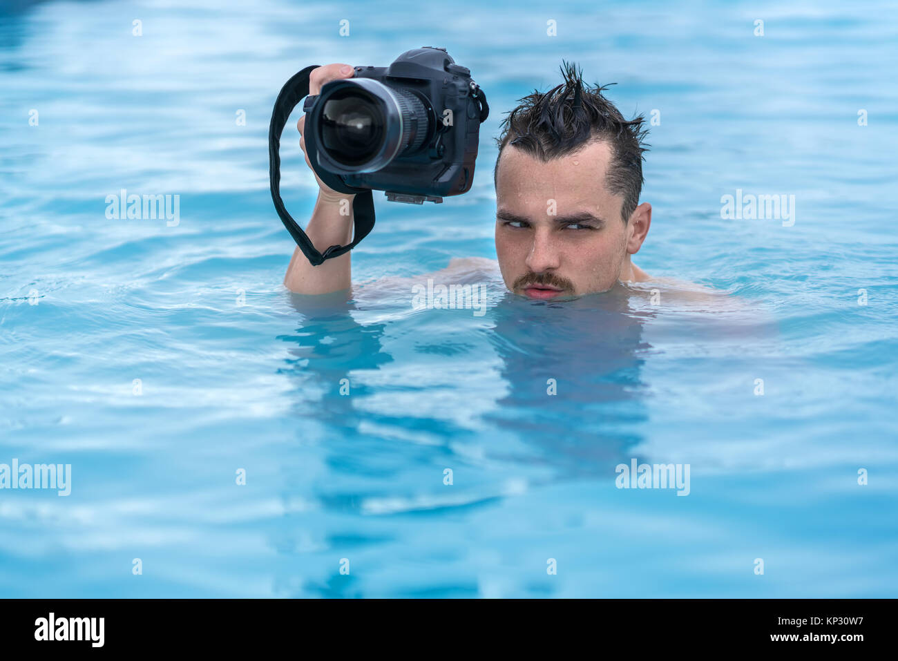 Funny guy holds a black camera in the geothermal pool outdoors in ...