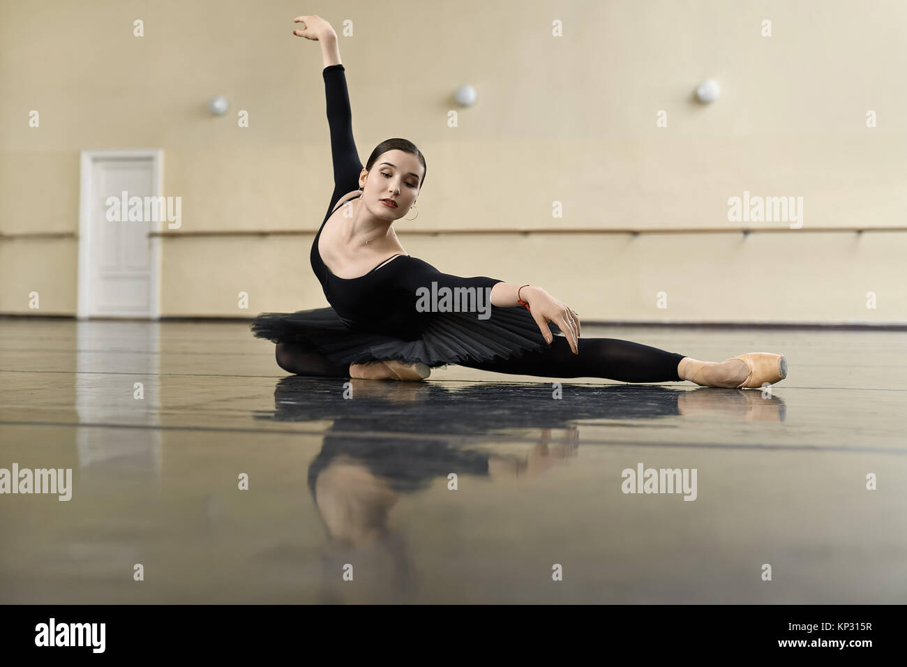 Gorgeous ballerina posing on the glossy floor in the dance hall. She is ...