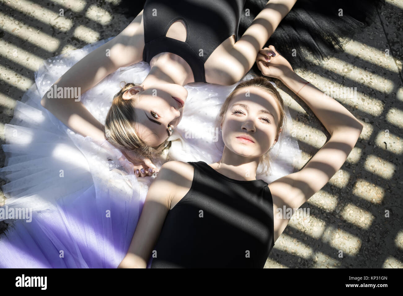 Ballet dancers lying on the tutus on the concrete floor outdoors. They ...