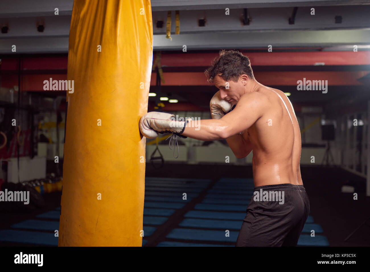 one young shirtless man, boxer hand hitting punching bag, practicing ...