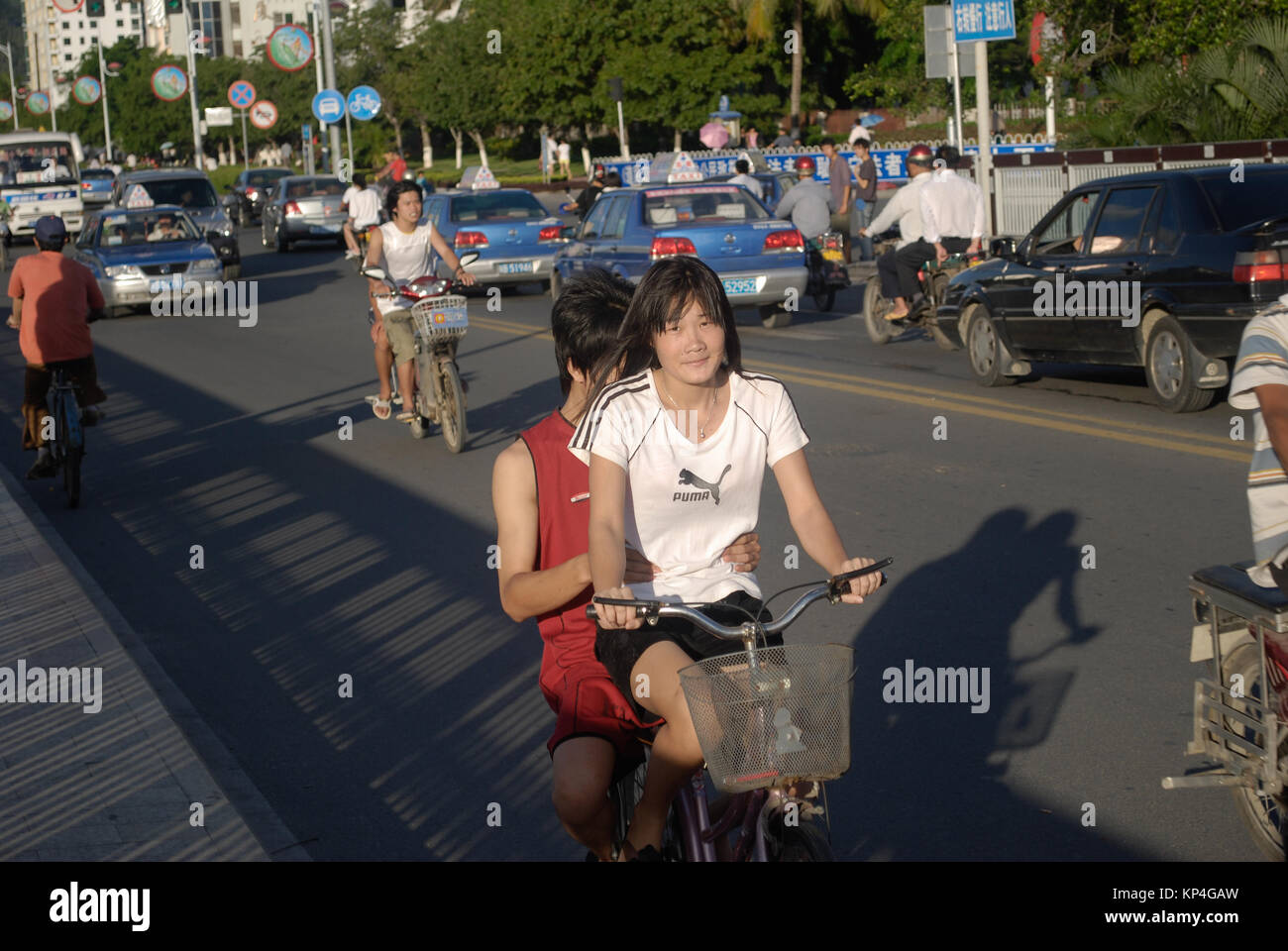 A girl rides a bicycle with a passenger in traffic in Sanya, Hainan ...