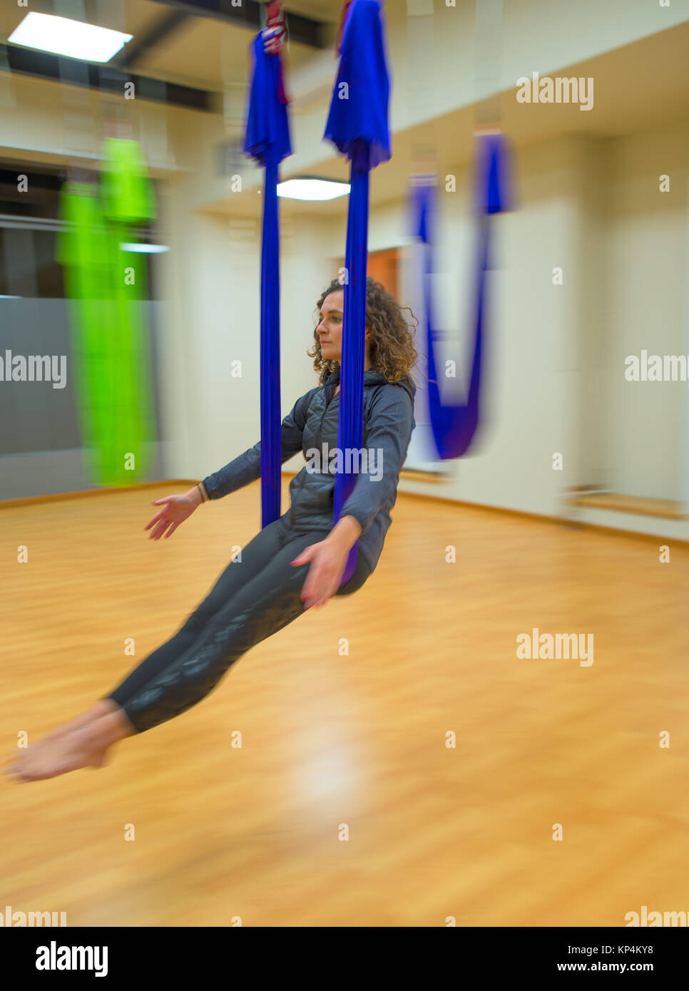 Pretty girl practices anti-gravity yoga position in gym swinging on a ...