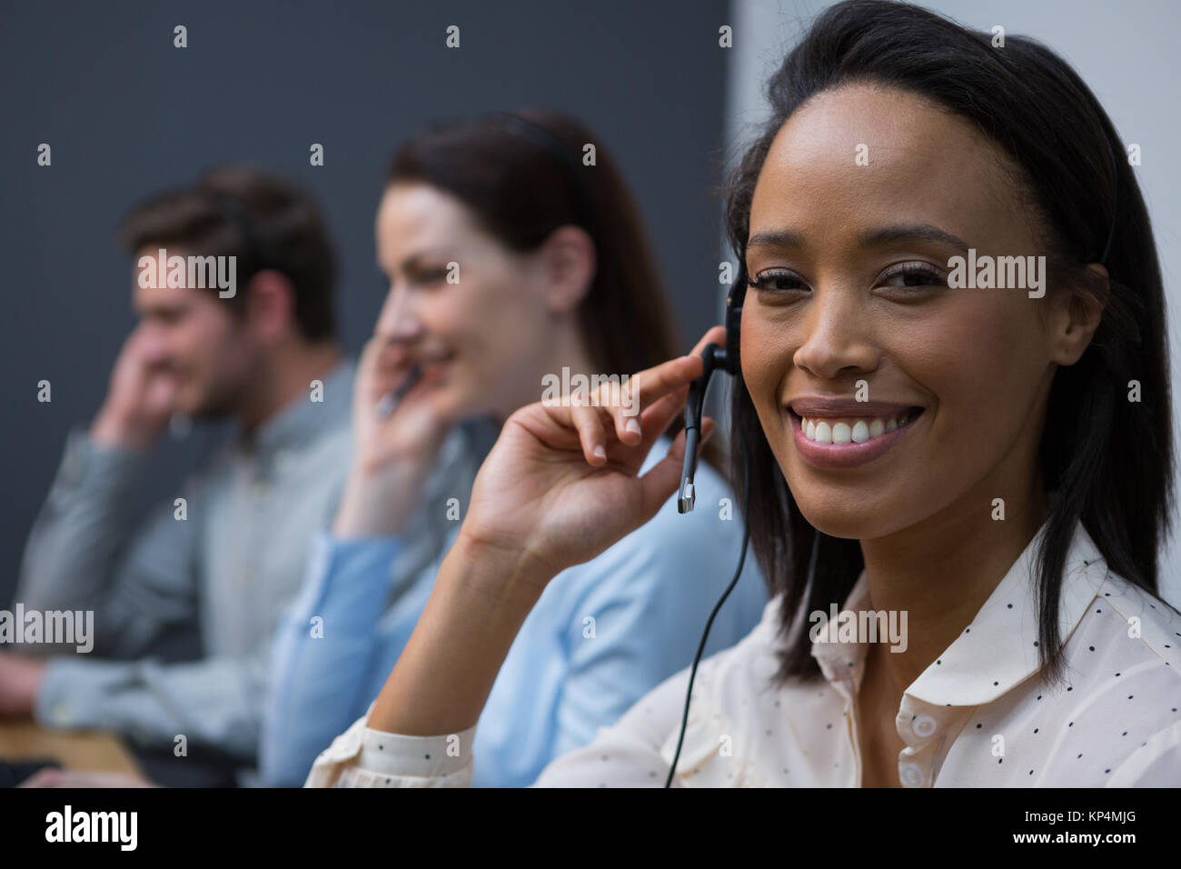 Business executives with headsets using computers at desk in office ...